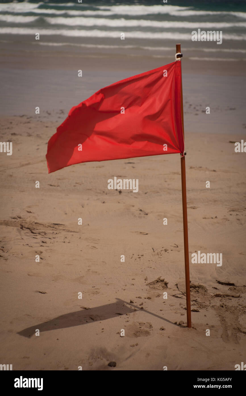 red flag flap on the beach, surfers in background Stock Photo - Alamy