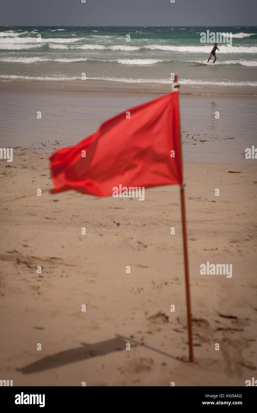red flag flap on the beach, surfers in background Stock Photo - Alamy