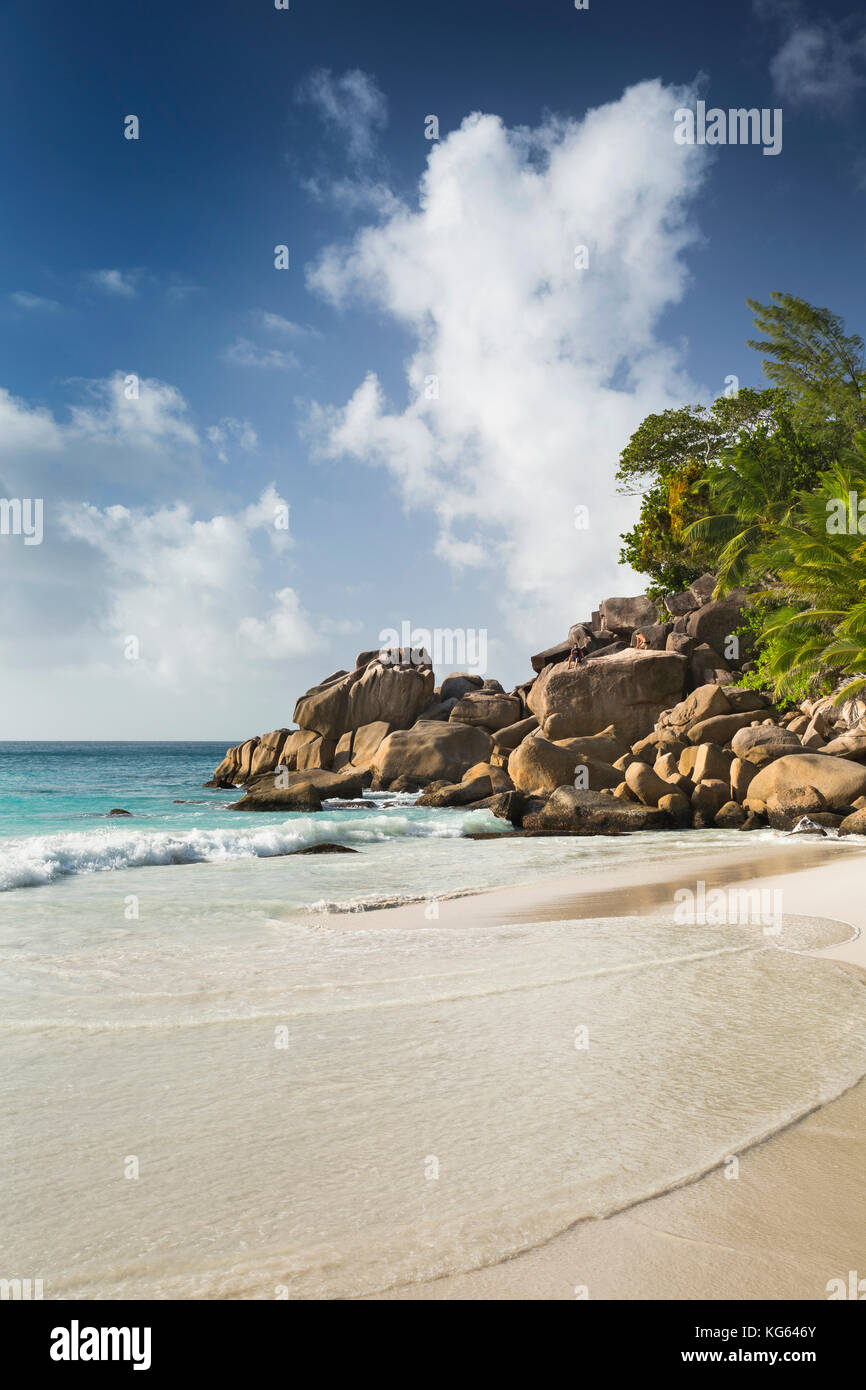The Seychelles, Praslin, Anse Georgette, beach man sat on rocks at edge ...