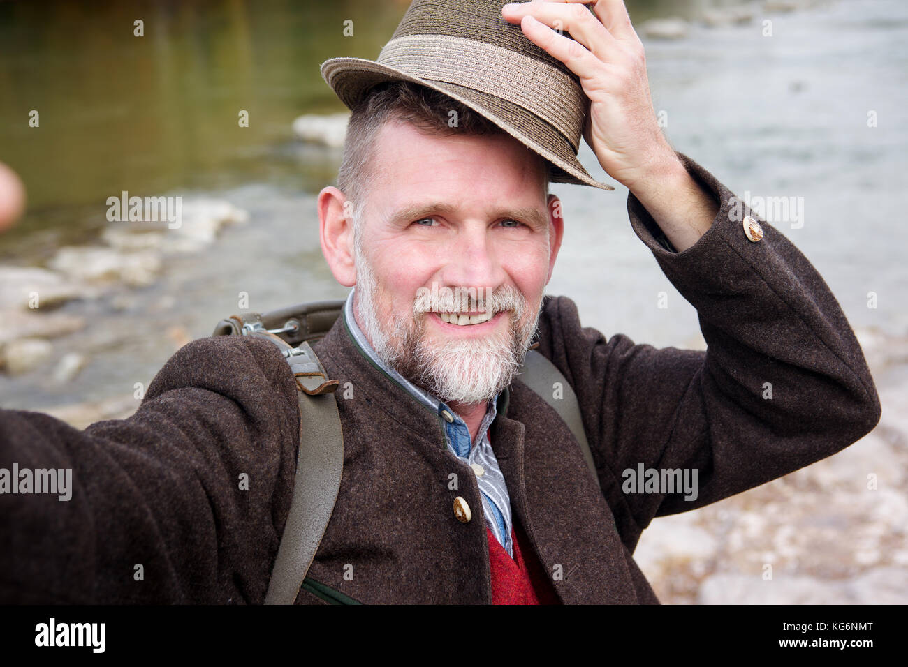 handsome bavarian man in his 50s standing by river and taking a selfie ...