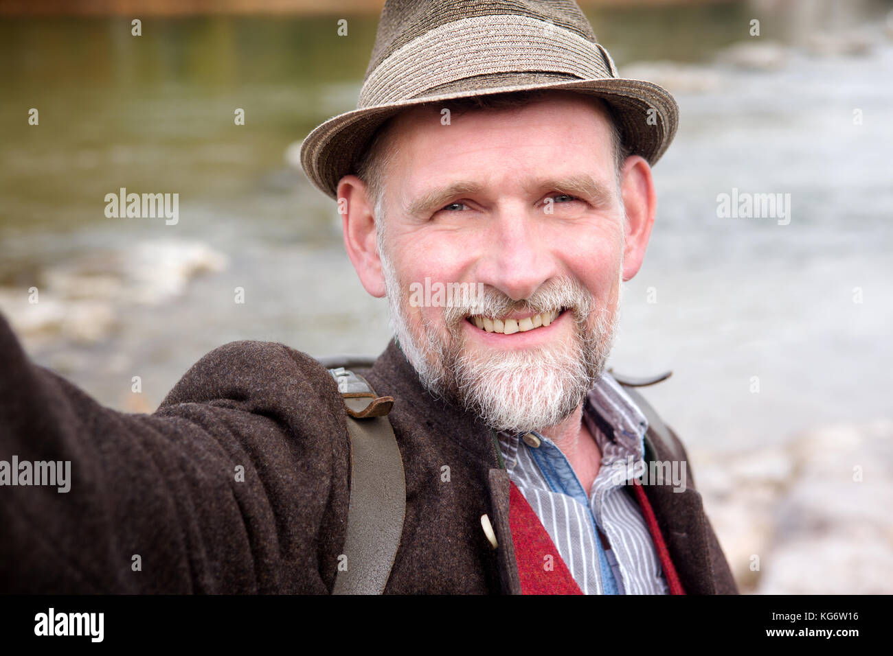 handsome bavarian man in his 50s standing by river and taking a selfie ...