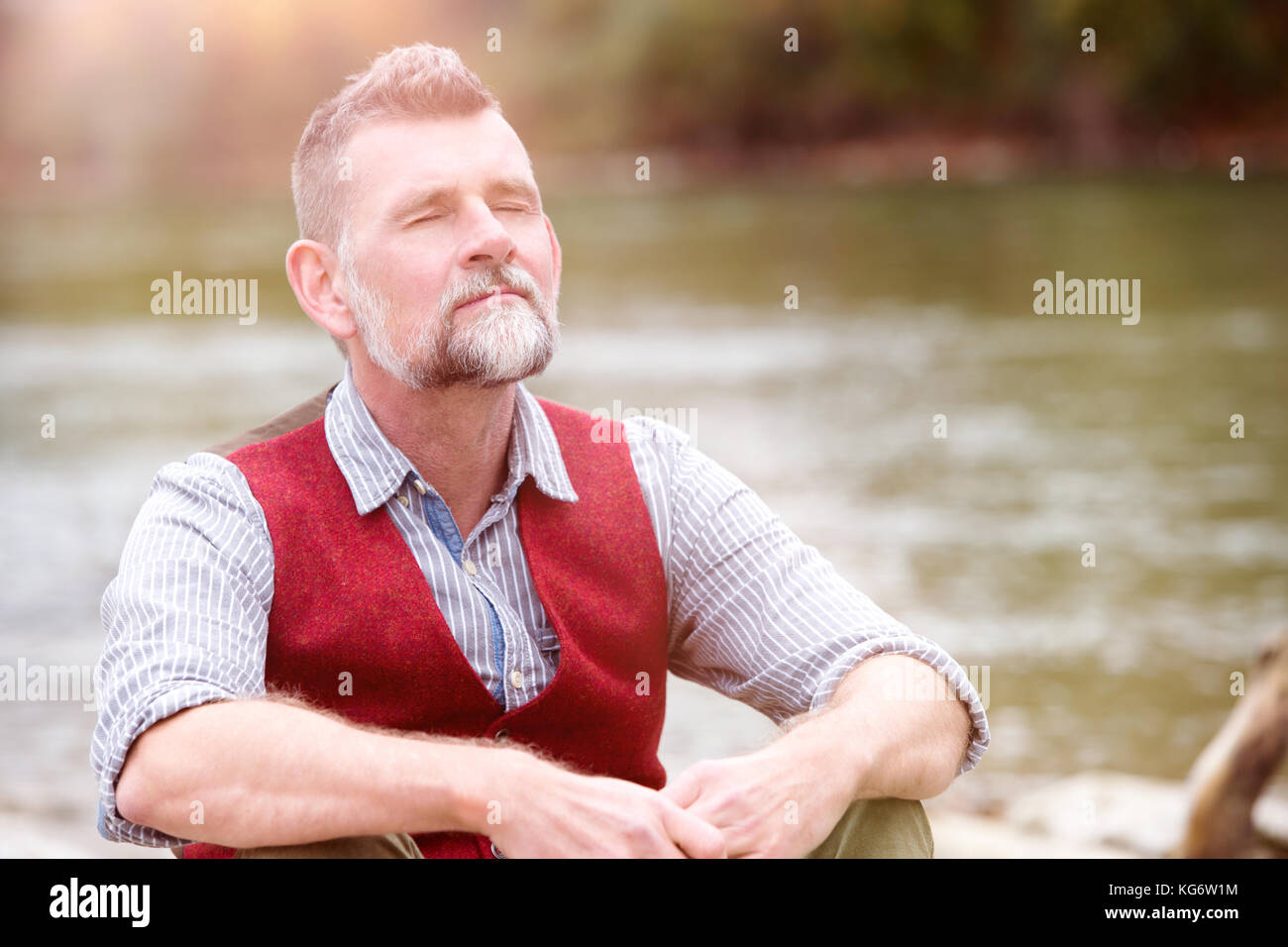 portrait of handsome man in his 50s sitting by the river in the sun ...