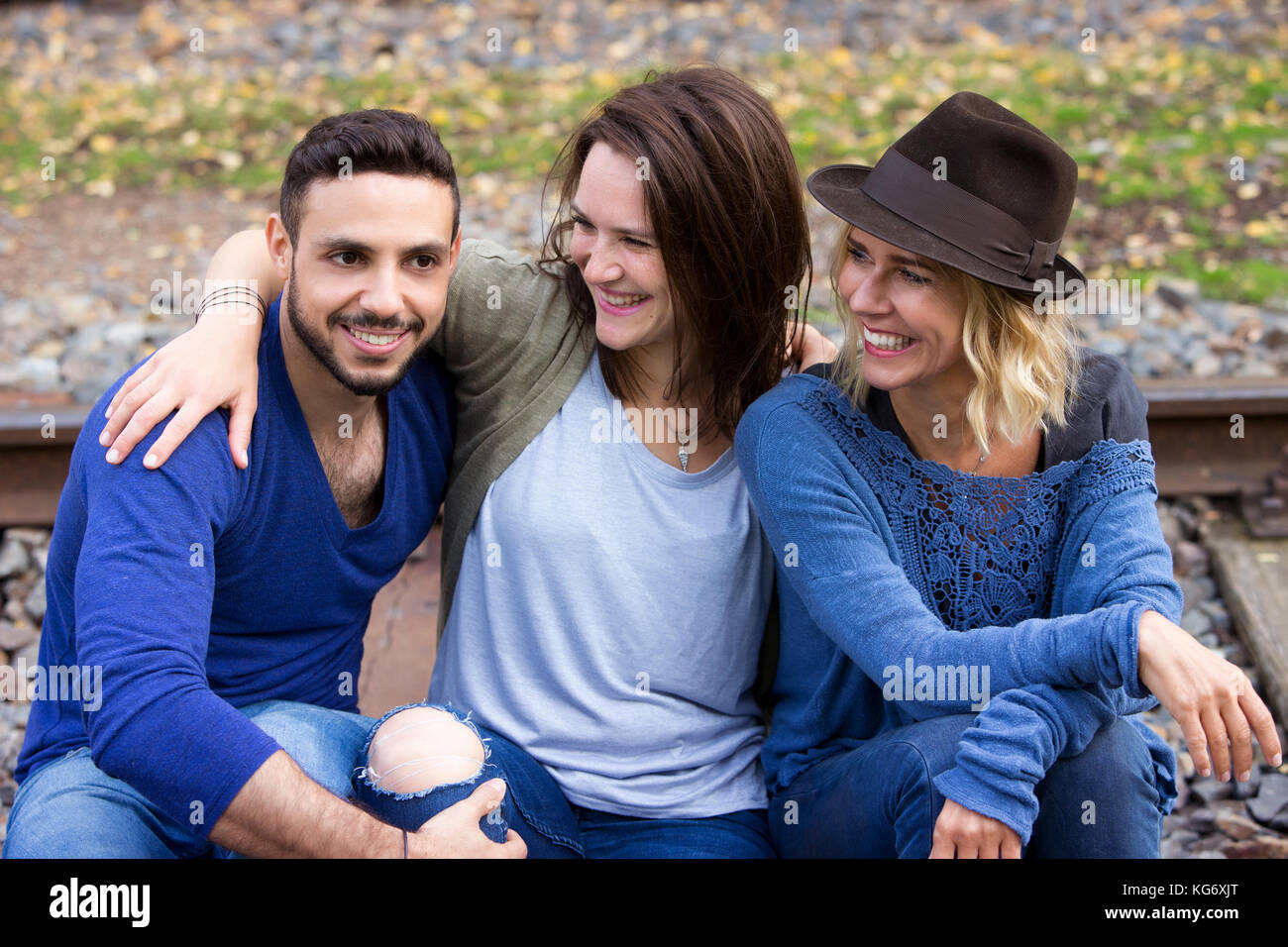 portrait of three friends sitting on train tracks and enjoying the sun ...