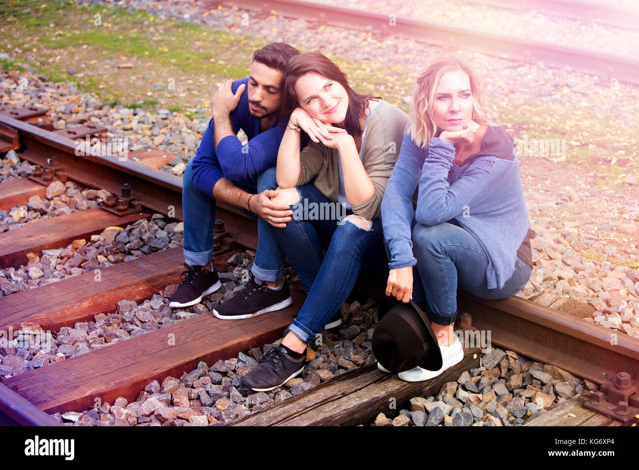 portrait of three friends sitting on train tracks and enjoying the sun ...