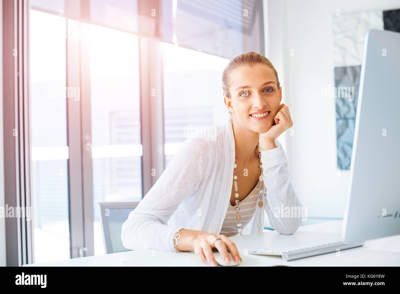 Attractive young woman sitting at desk and working on her computer ...