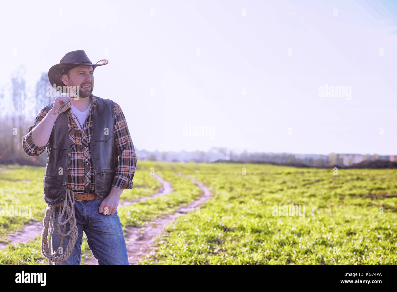 Cowboy in a hat and with a lasso standing in a field at sunset Stock ...