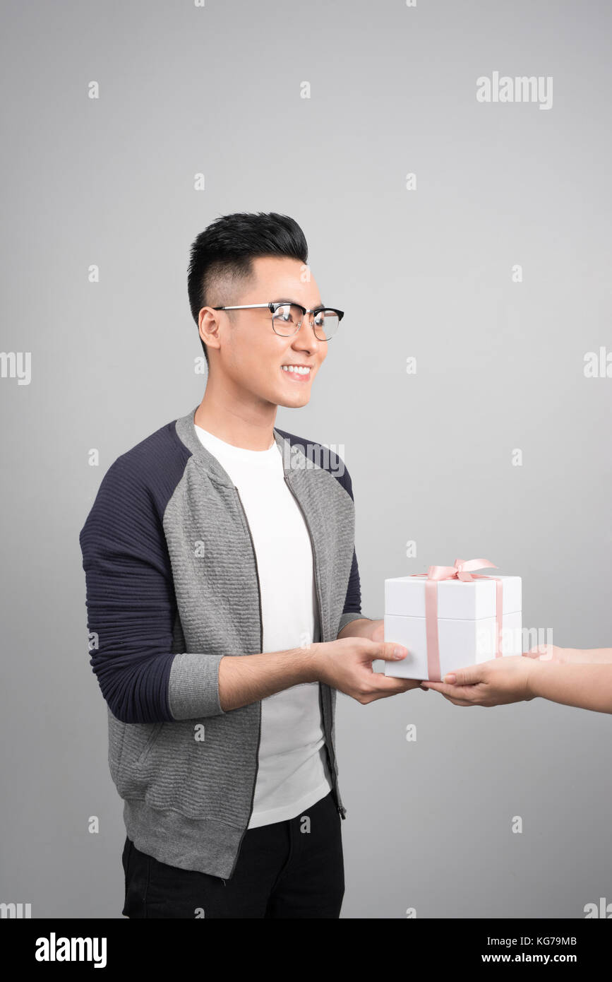 Happy young asian man giving gift box over gray background Stock Photo ...