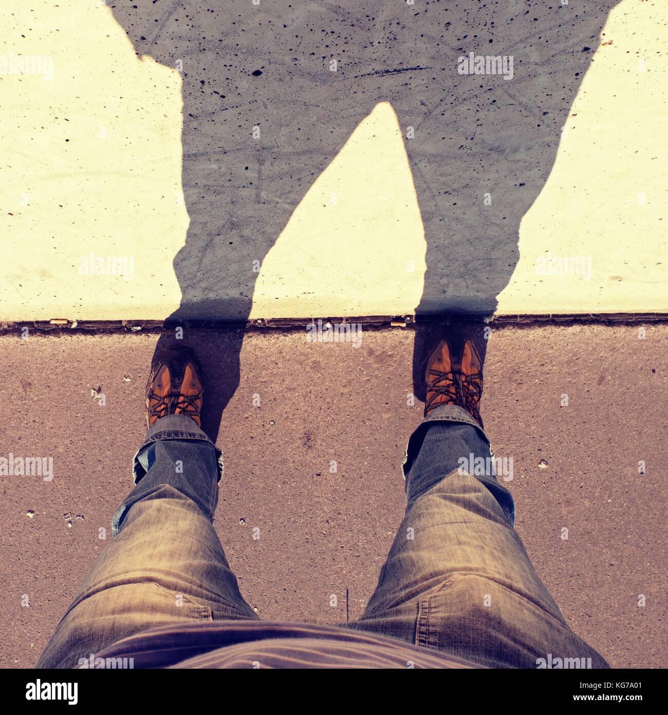 Man long legs stand on street at concrete wall with strong shadow ...