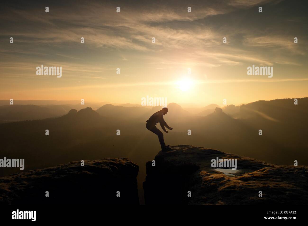 Crazy hiker in black is jumping between rocky peaks. Happy man ...