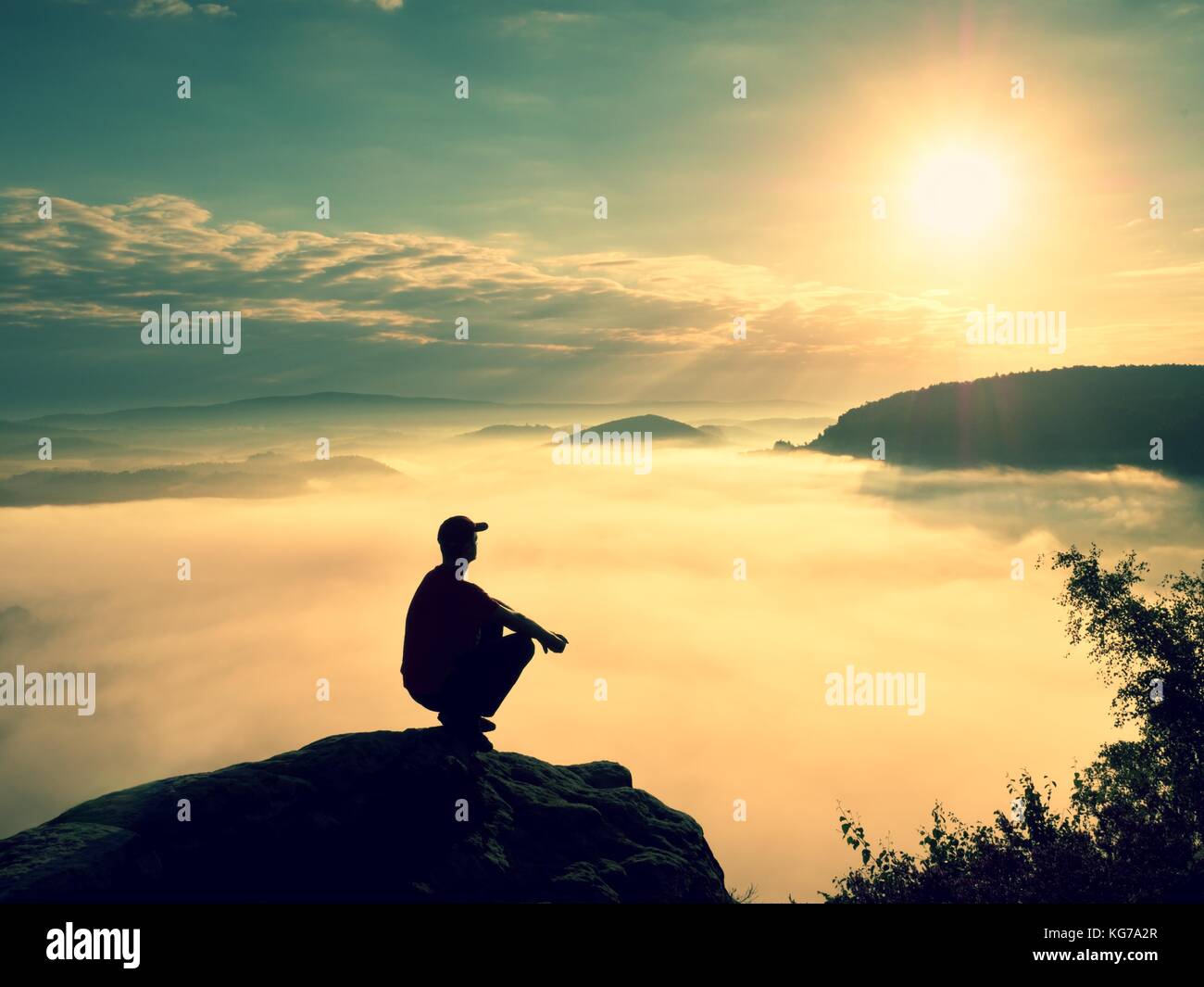 Moment of loneliness. Man sit on rock and watching into colorful mist ...