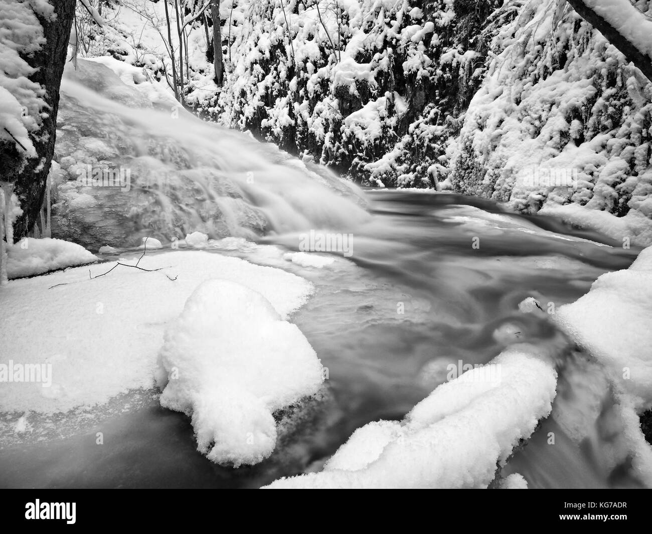Frozen cascade of waterfall, icy twigs and icy boulders in frozen foam ...