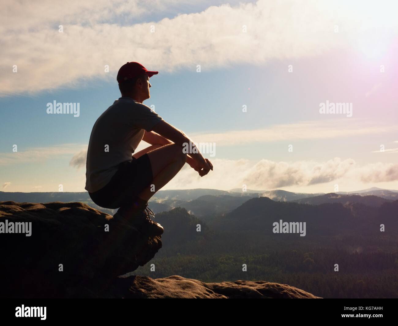 Man tourist sit on exposed rock. View point with sharp rock above misty ...