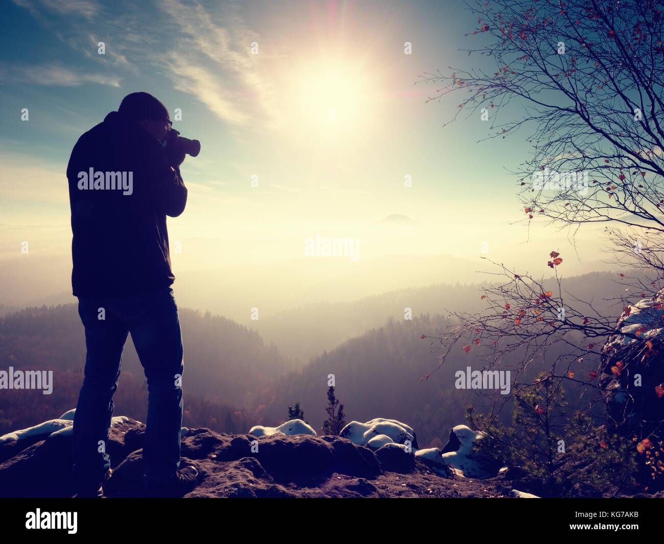 Tall man is taking photo by mirror camera on neck. Snowy rocky peak of ...