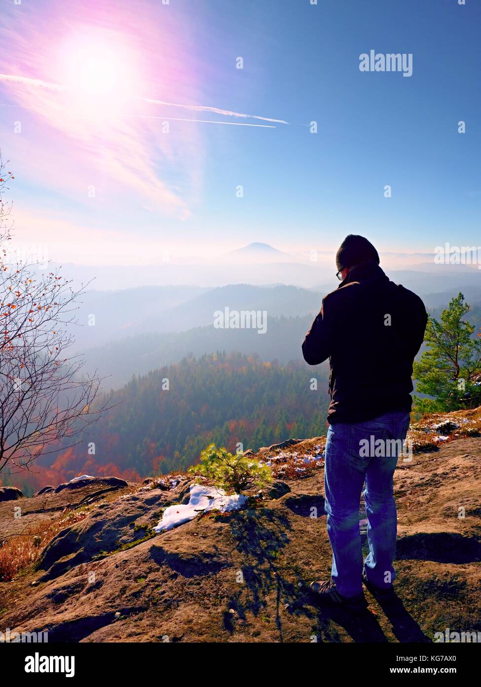 Tall man is taking photo by mirror camera on neck. Snowy rocky peak of ...