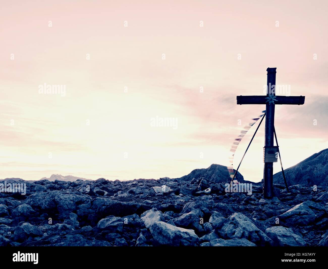 Modest wooden cross with Buddhist praying flags, raised on rocky Alpine ...