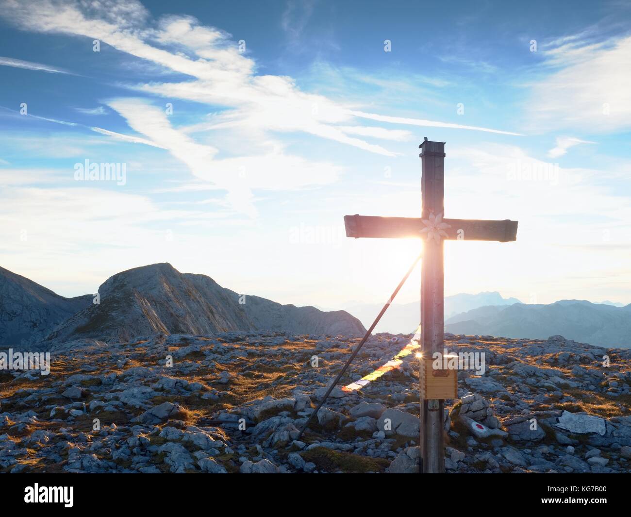 Modest wooden cross with Buddhist praying flags, raised on rocky Alpine ...