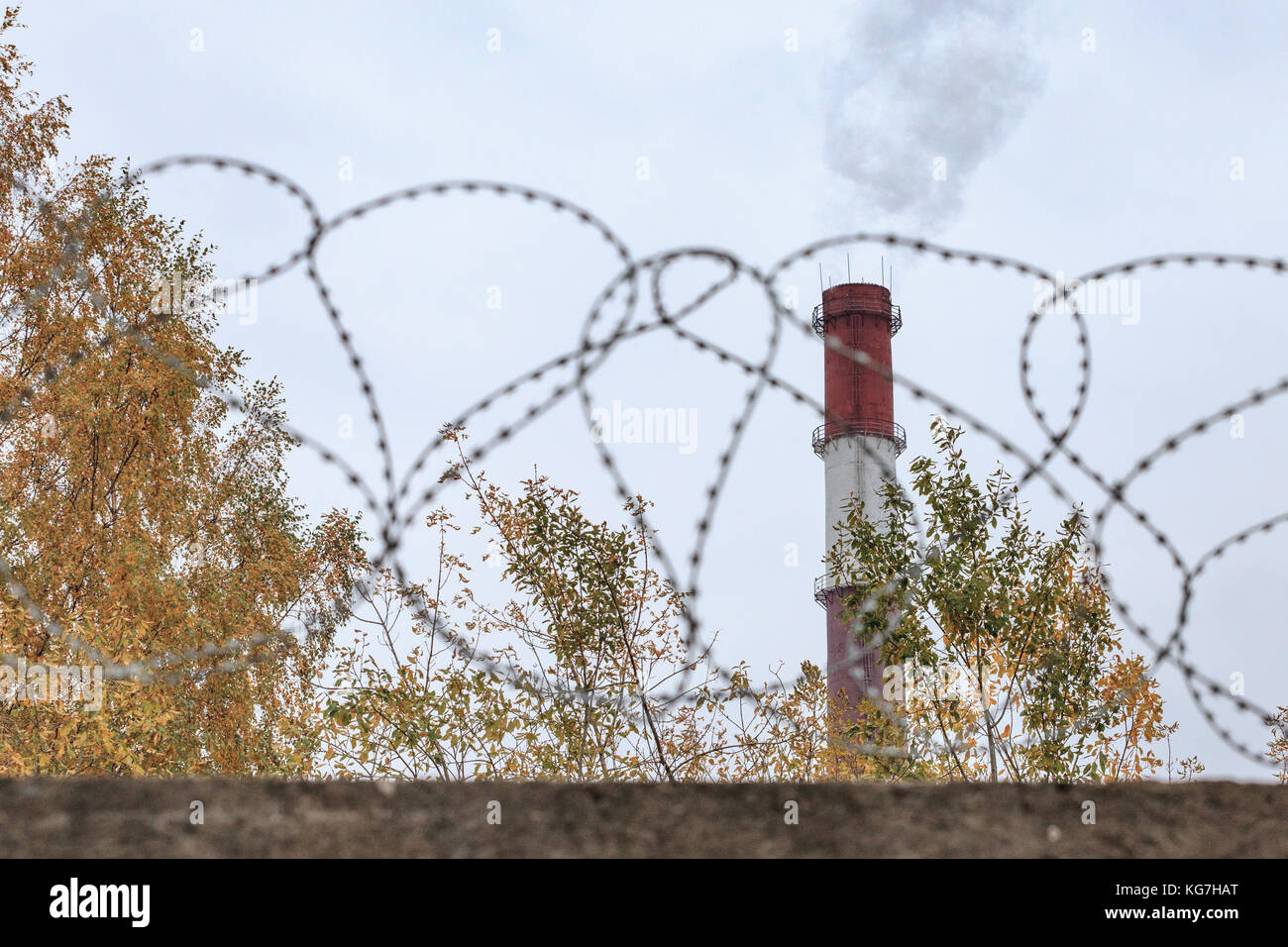 A pipe with smoke behind a fence with barbed wire Stock Photo - Alamy
