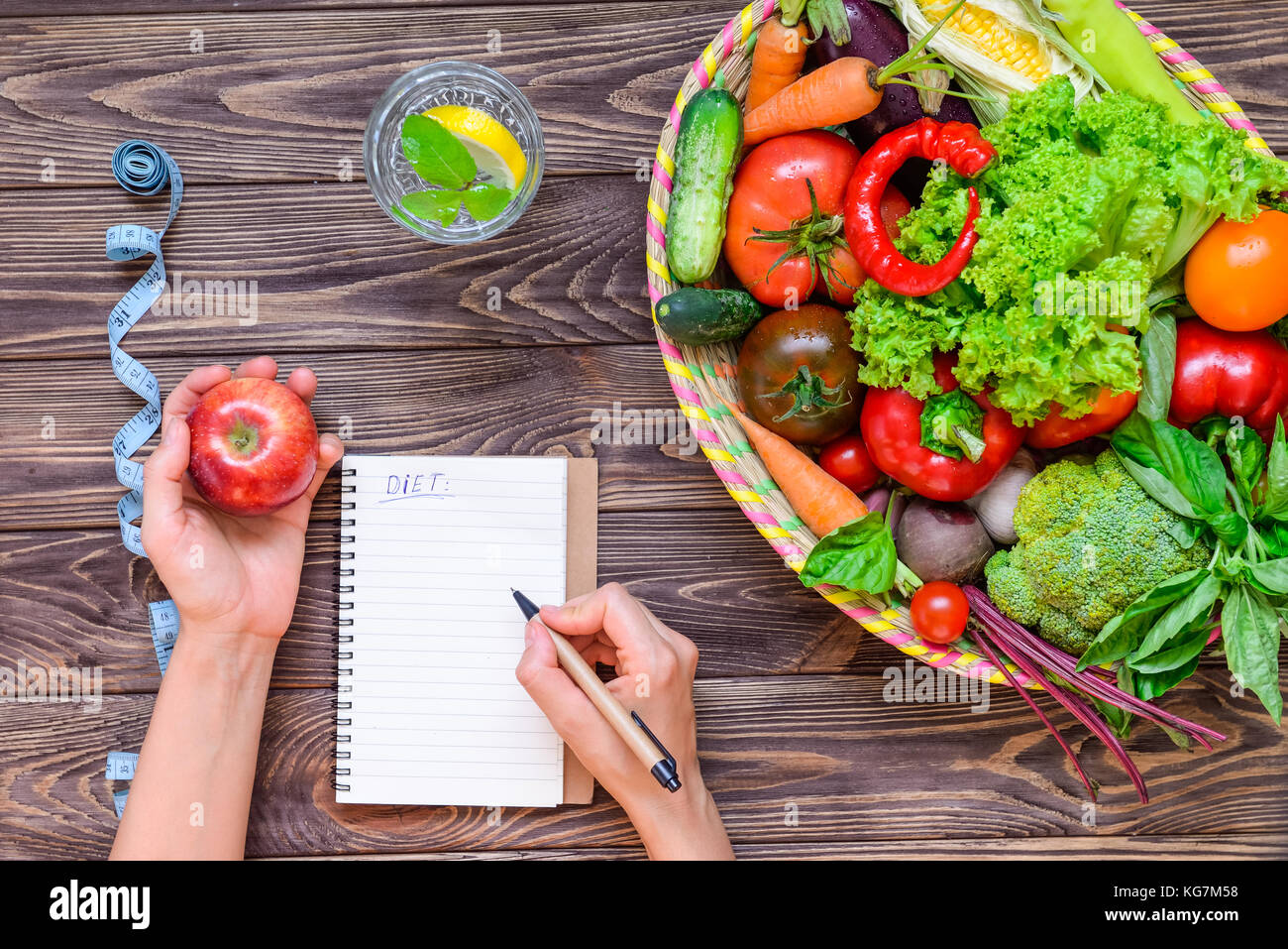 Female hands make notes in diet book on the wood table with Basket of ...