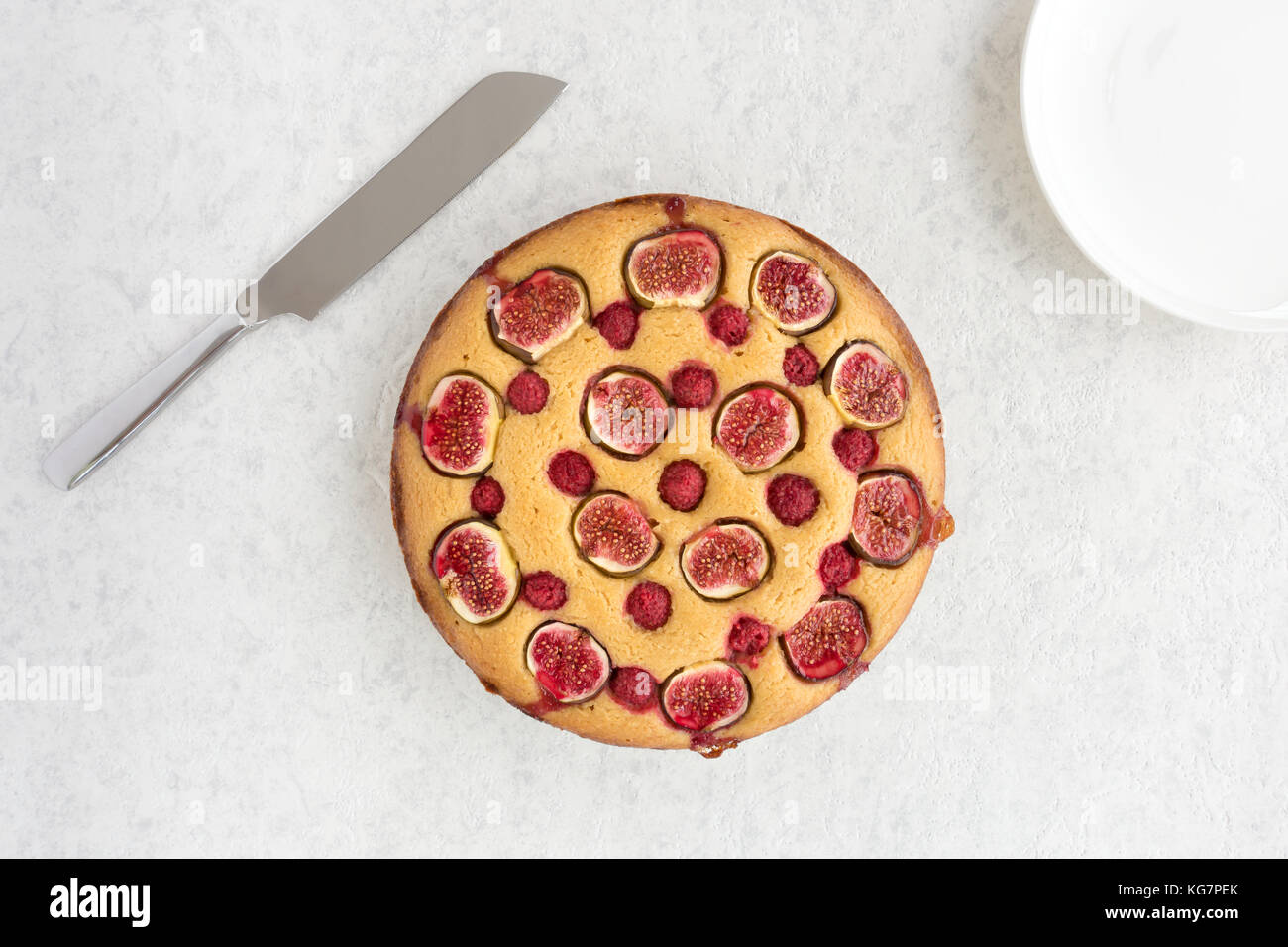 Homemade fig and raspberry cake with cake knife and plate on white ...