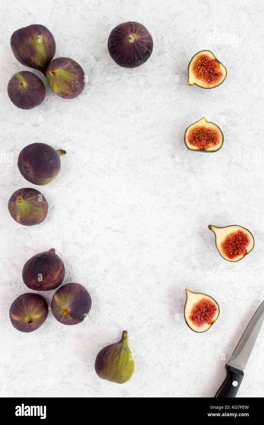 Whole and halved figs and a knife on a white marbled background with ...