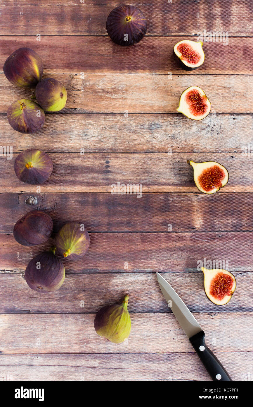 Whole and halved figs and a knife on a dark brown wood background with ...
