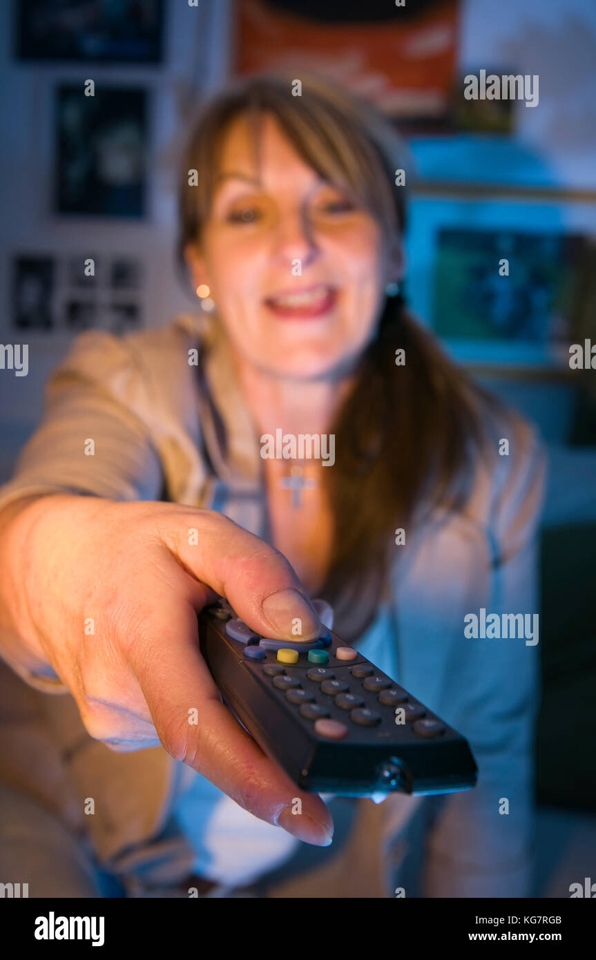 Frontal view of a middle-aged woman with remote control smiling towards ...