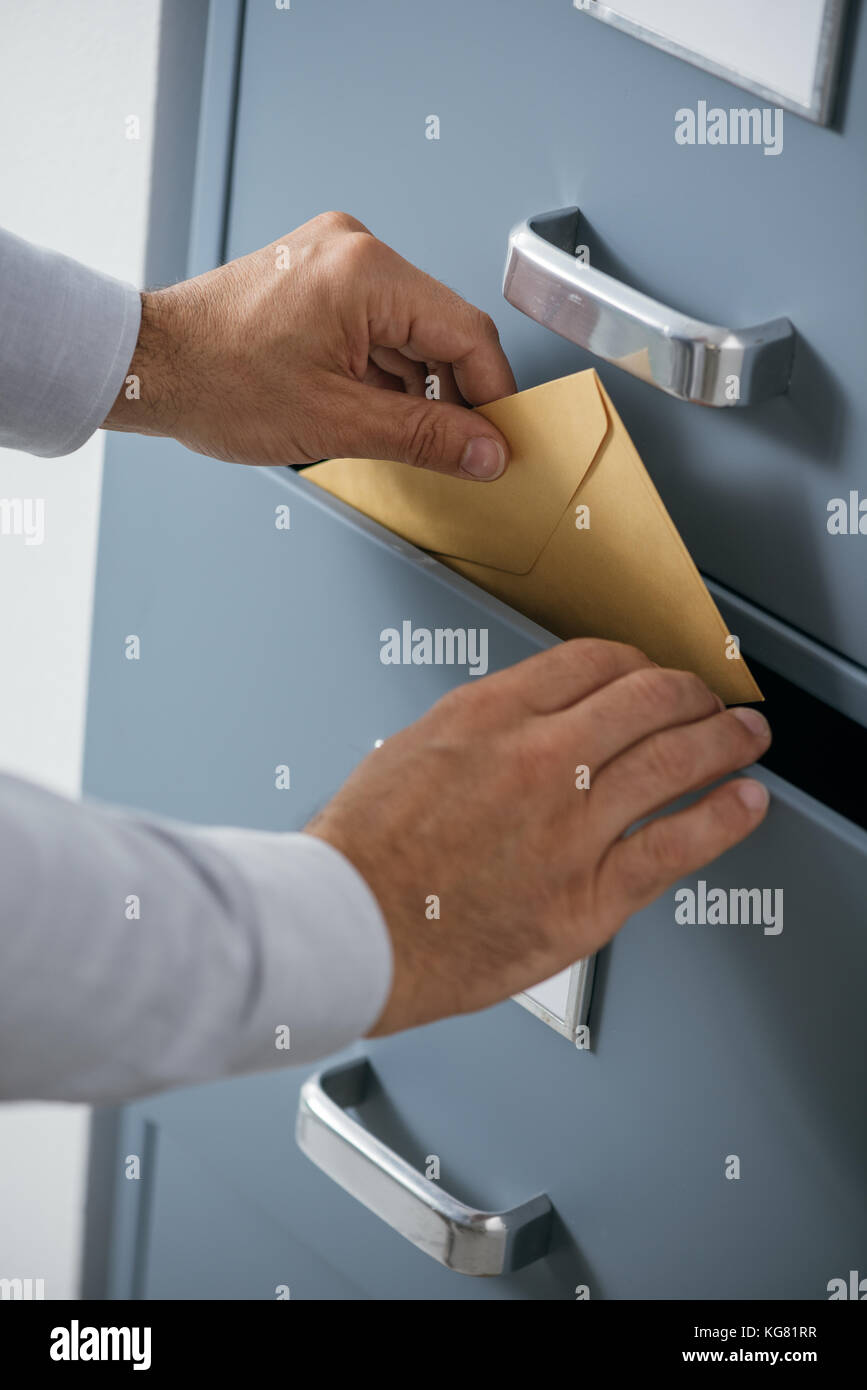Businessman putting a closed envelope into a filing cabinet's drawer ...