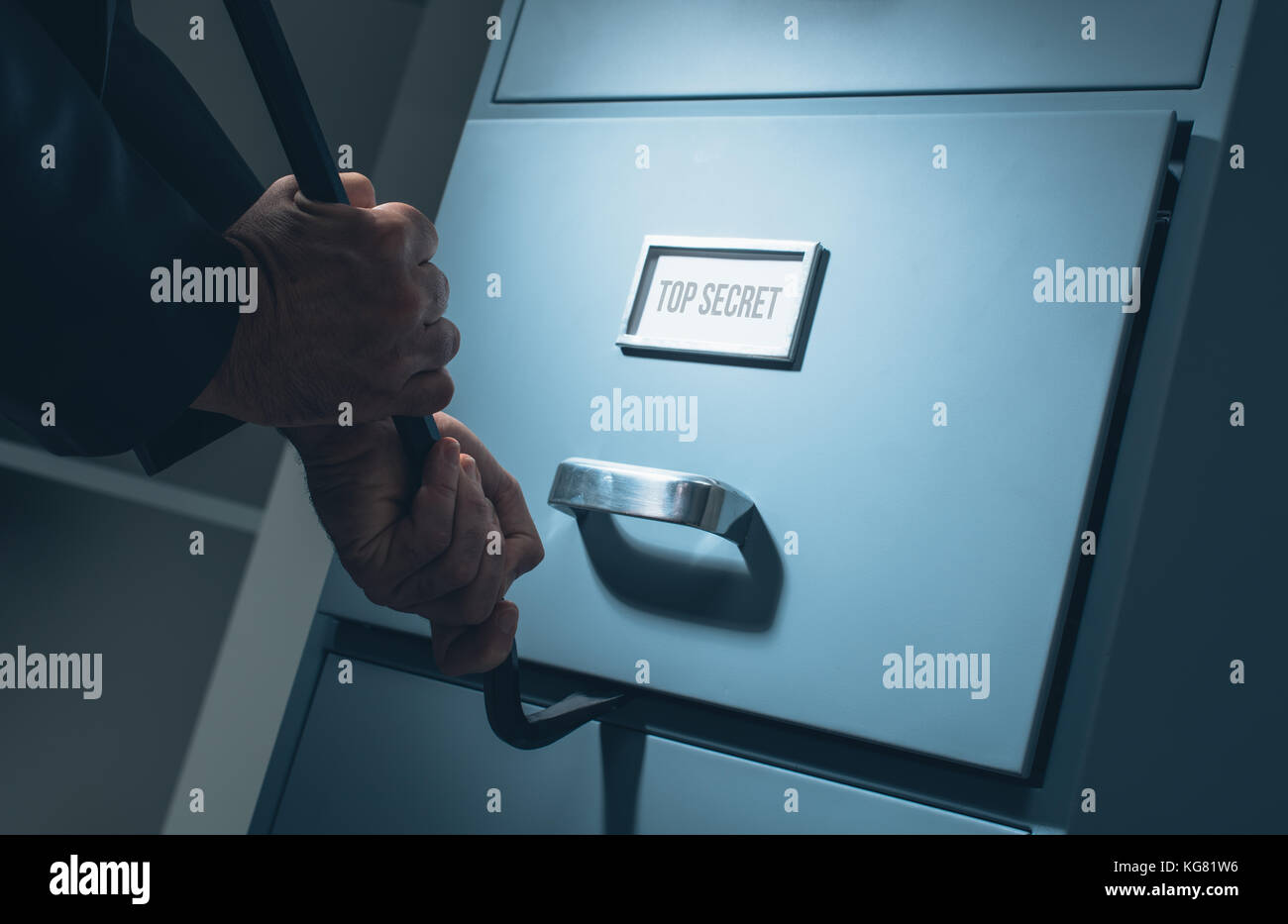 Burglar opening a drawer in the office at night using a crowbar, he is ...