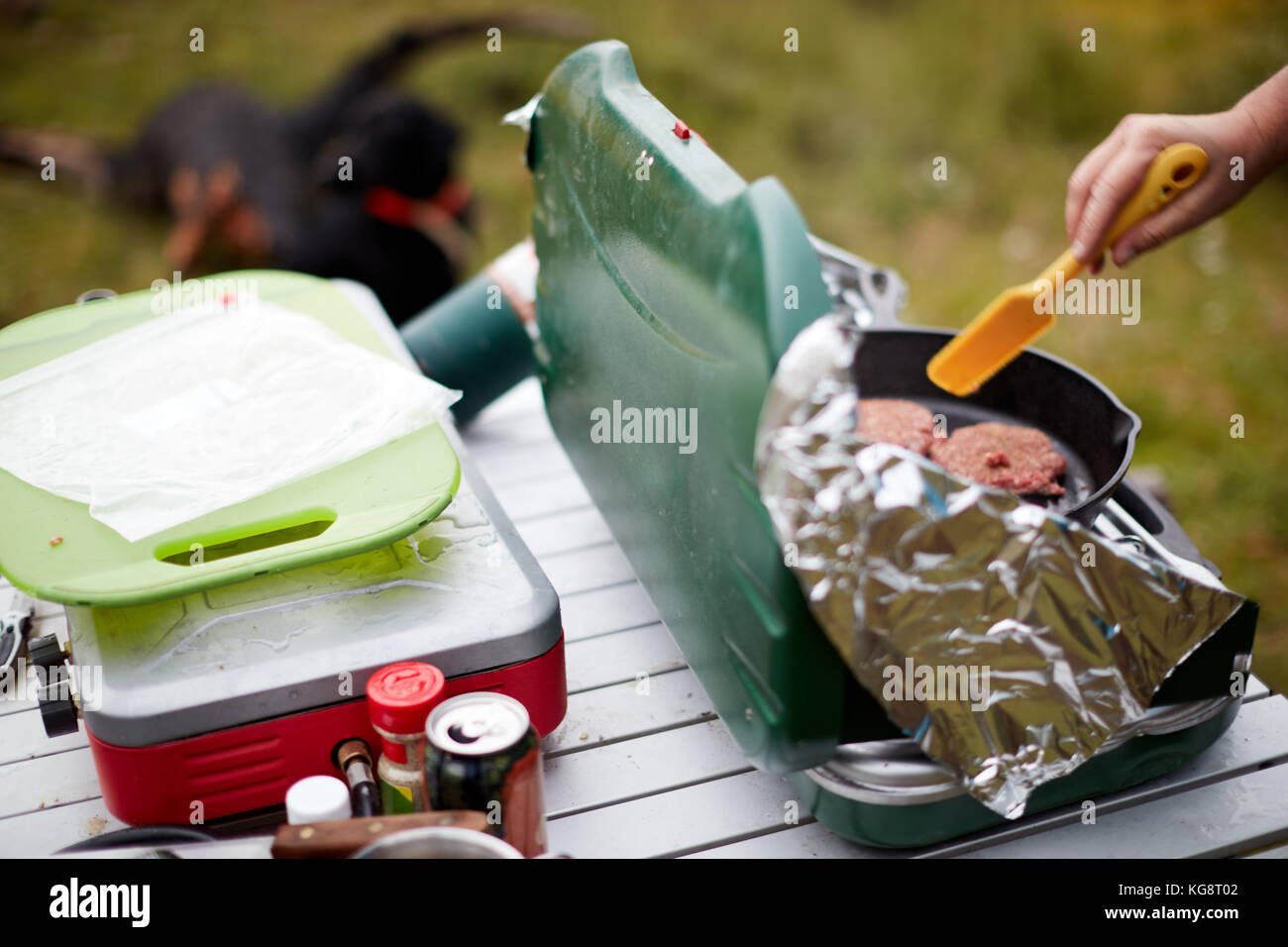 Man cooking raw burger patties on a camping gas stove outdoors on a ...