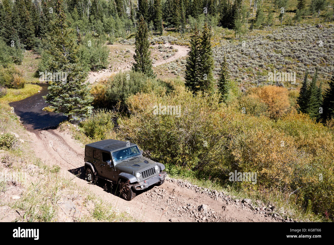 4WD vehicle driving through rugged terrain along a narrow dirt road ...