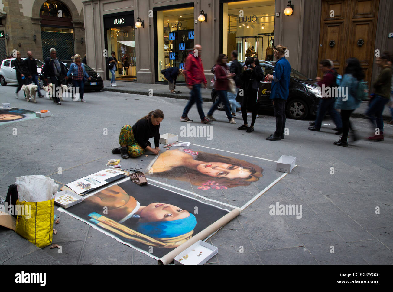 Street artist doing a chalk drawing on the pavement with passersby ...