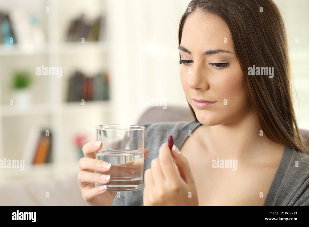 Serious lady ready to take a red pill sitting on a sofa in the living ...