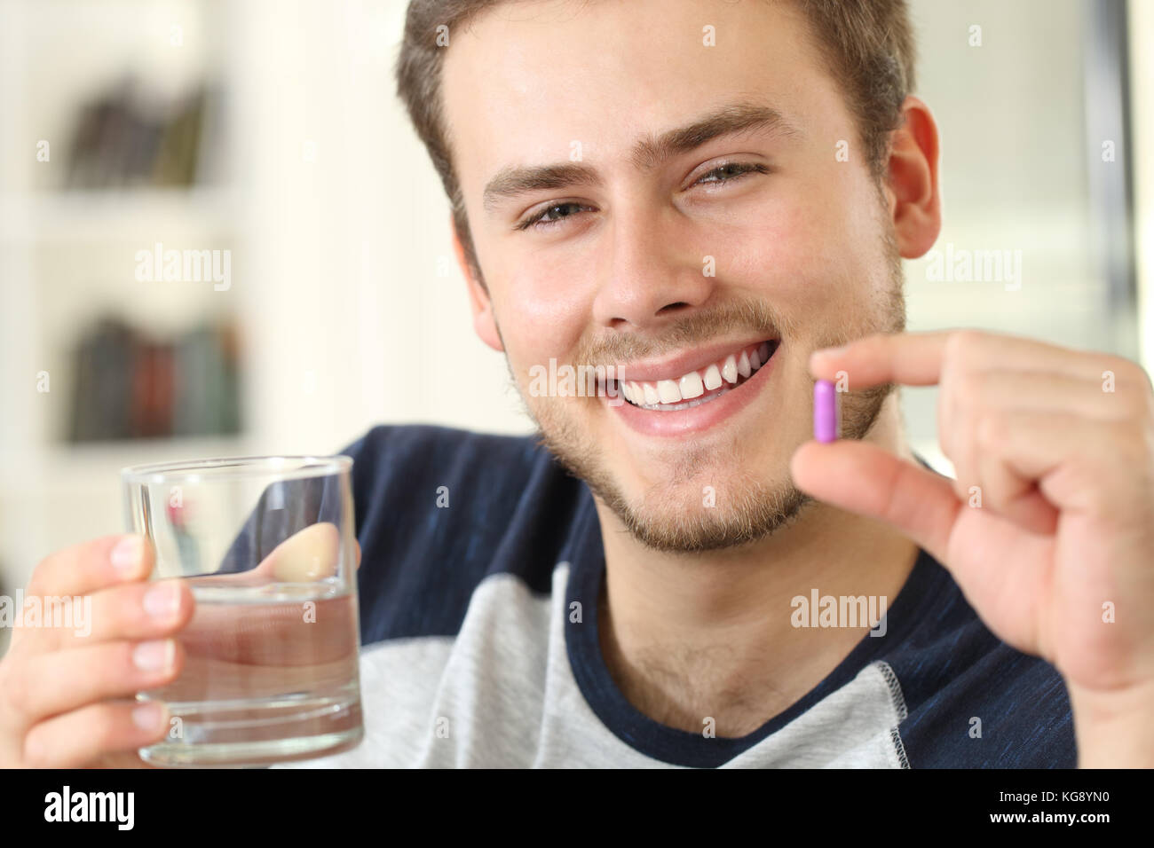 Happy man holding a pink pill and a glass of water looking at camera ...