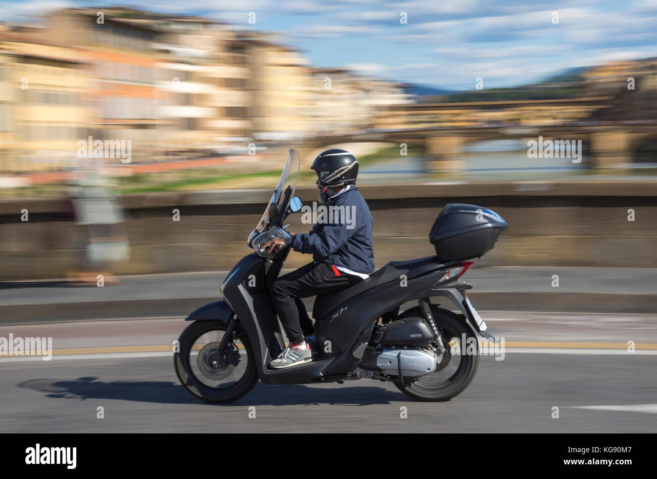 Moped rider driving over a bridge with the Ponte Vecchio in the ...