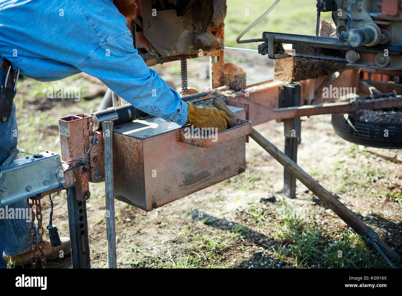 Workman at a sawmill adjusting a milling machine as he mills a piece of ...