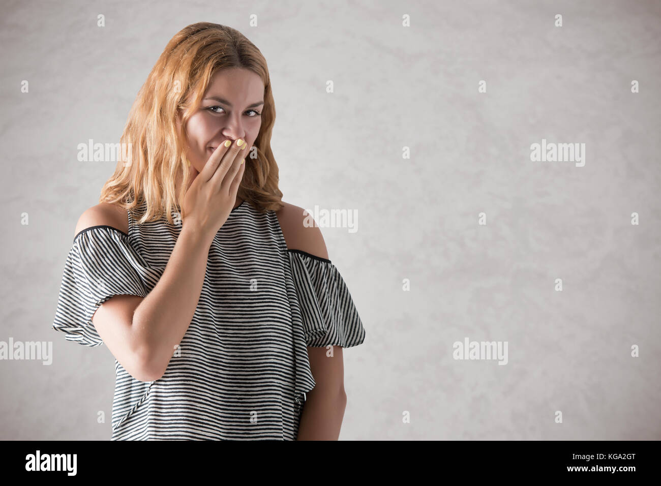 Shy girl covering up her face with her hands, in a grey background ...