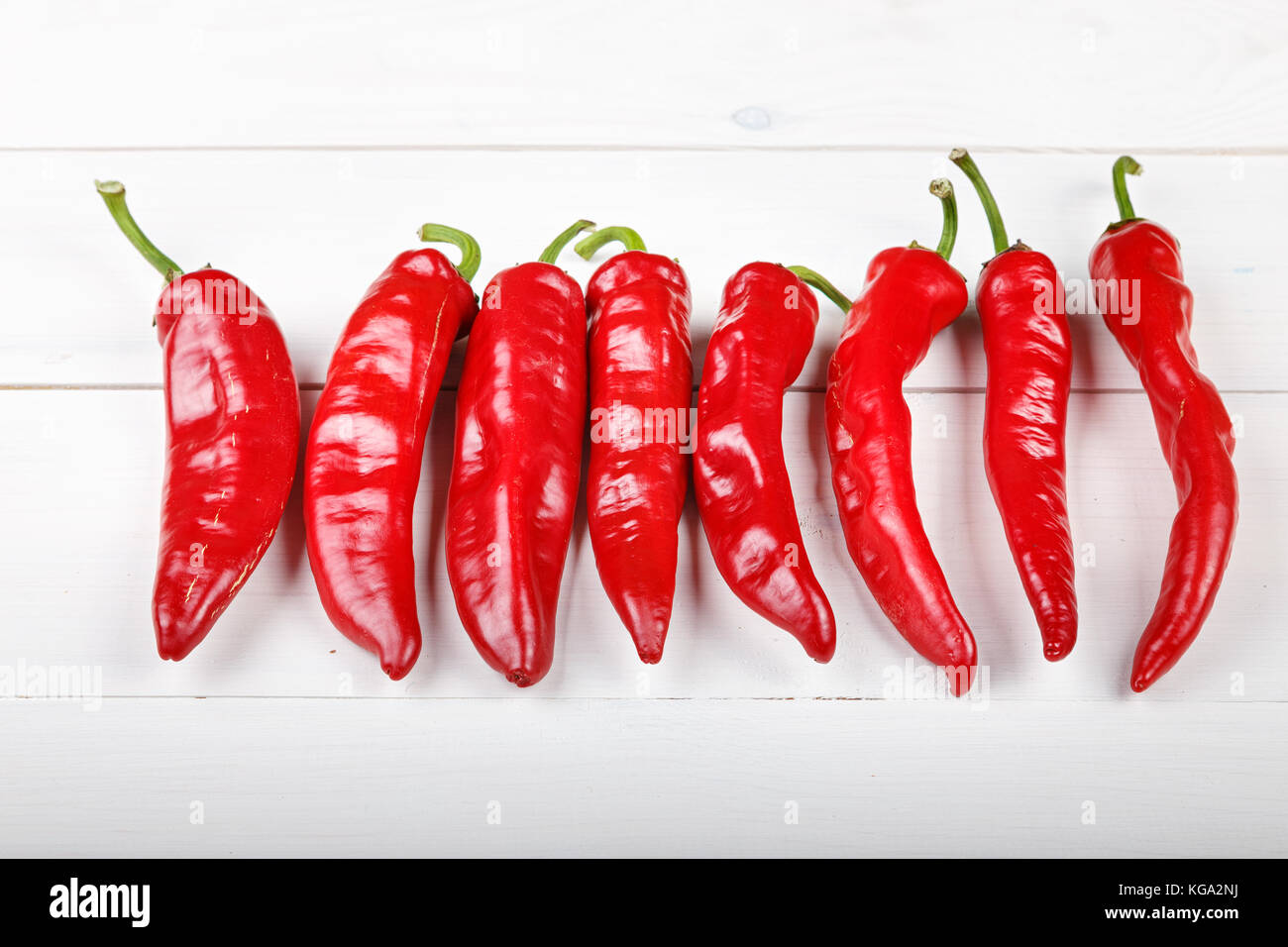 Red chilli pepper in a row on a white wooden background, horizontal ...