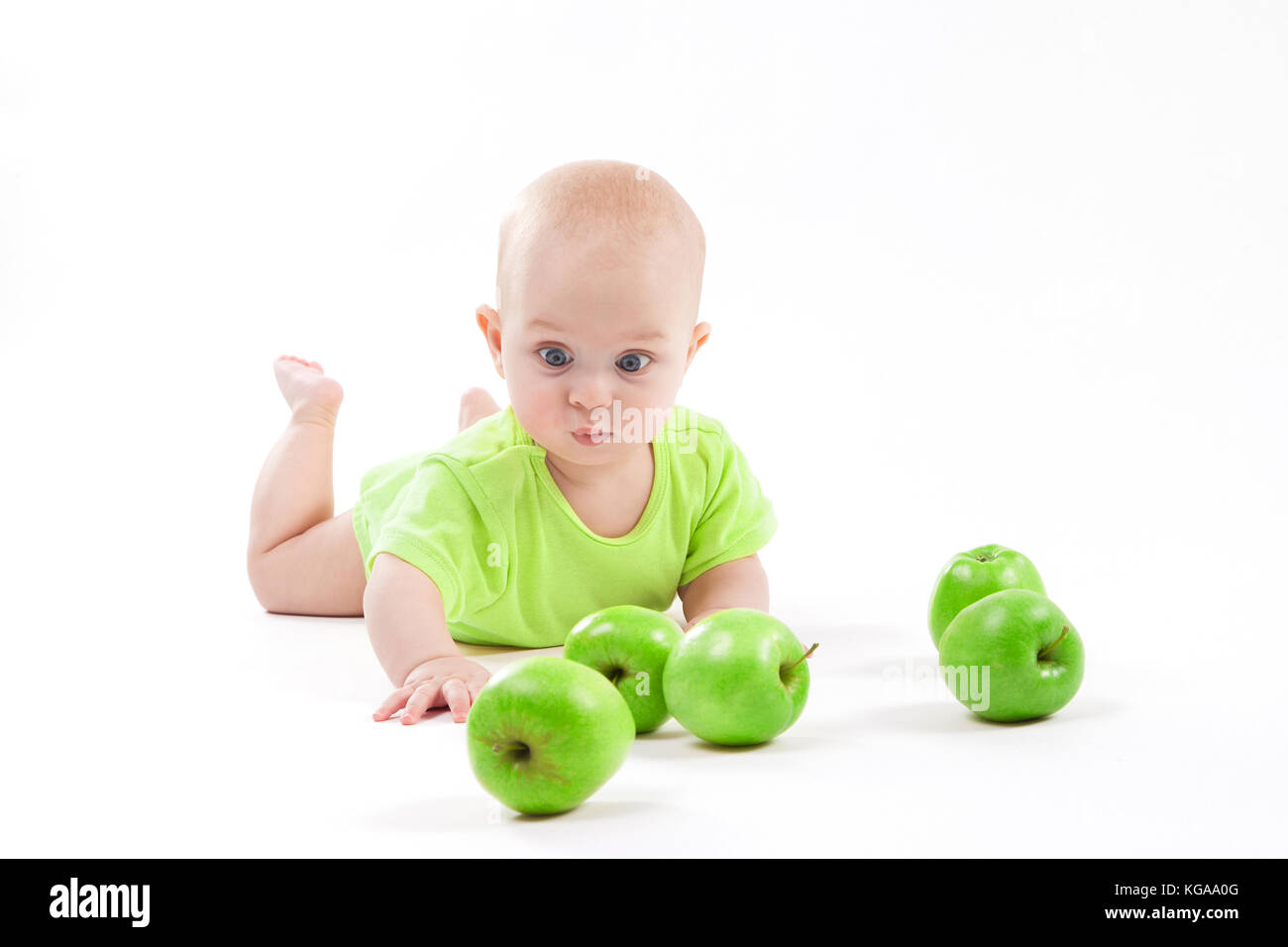 cute surprised baby looks at green apple on a white background Stock ...