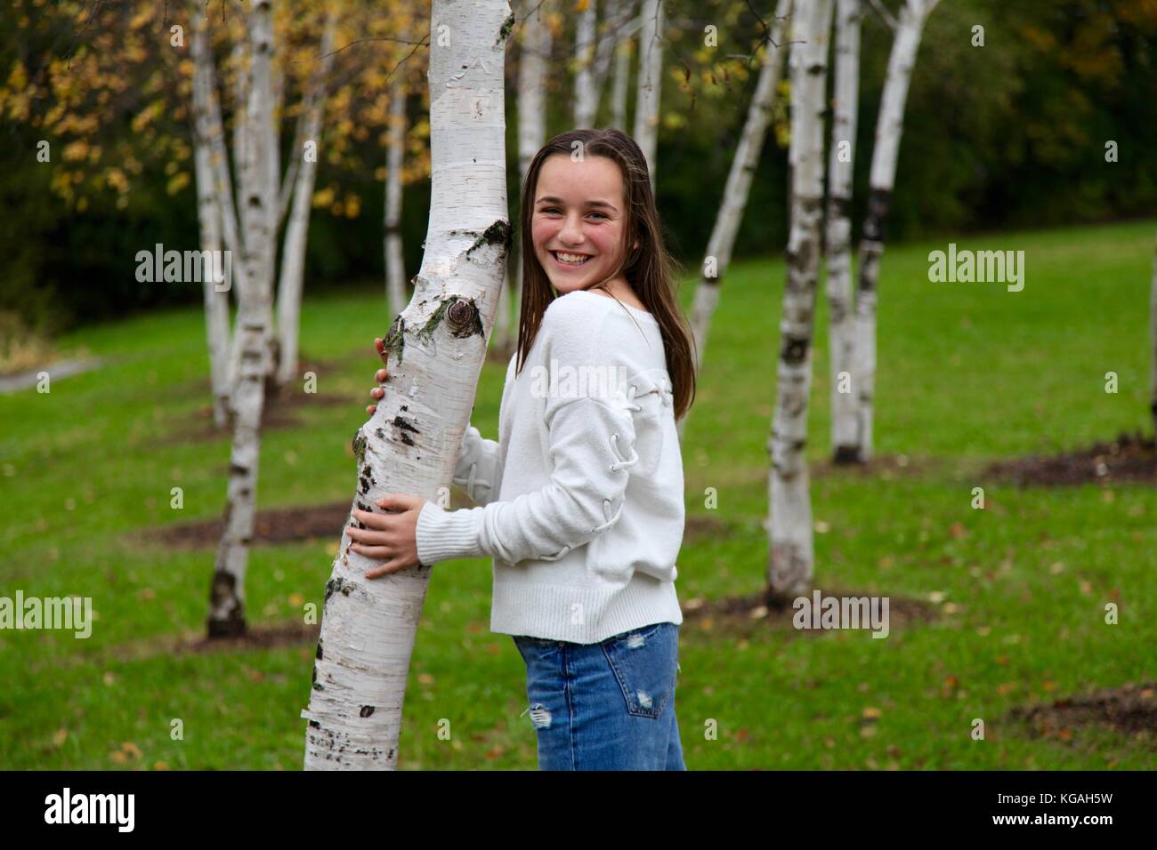 Portrait of a young teenage girl smiling and hugging a birch tree ...