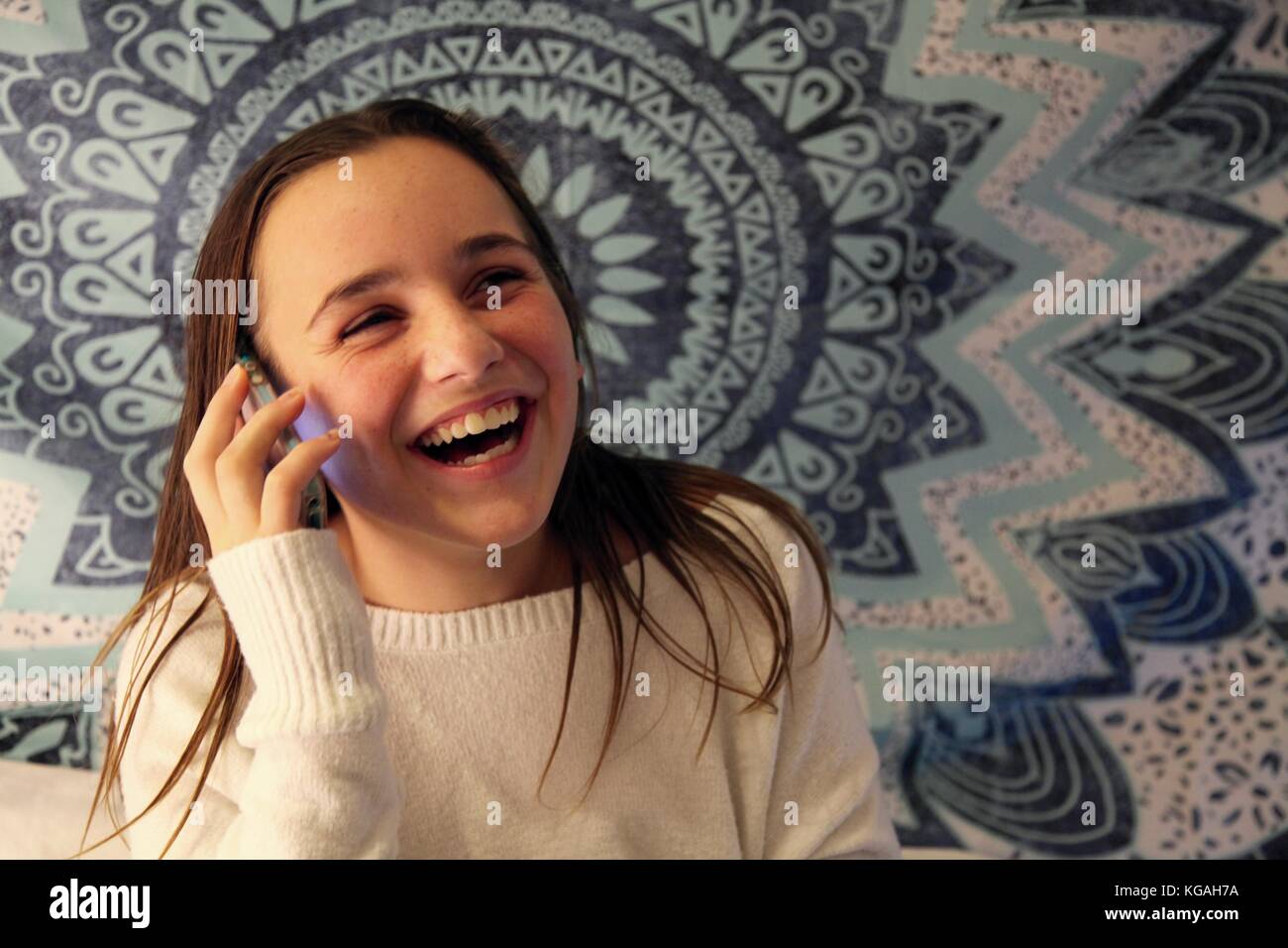 Young teenage girl laughing as she talks on the phone with her friend ...
