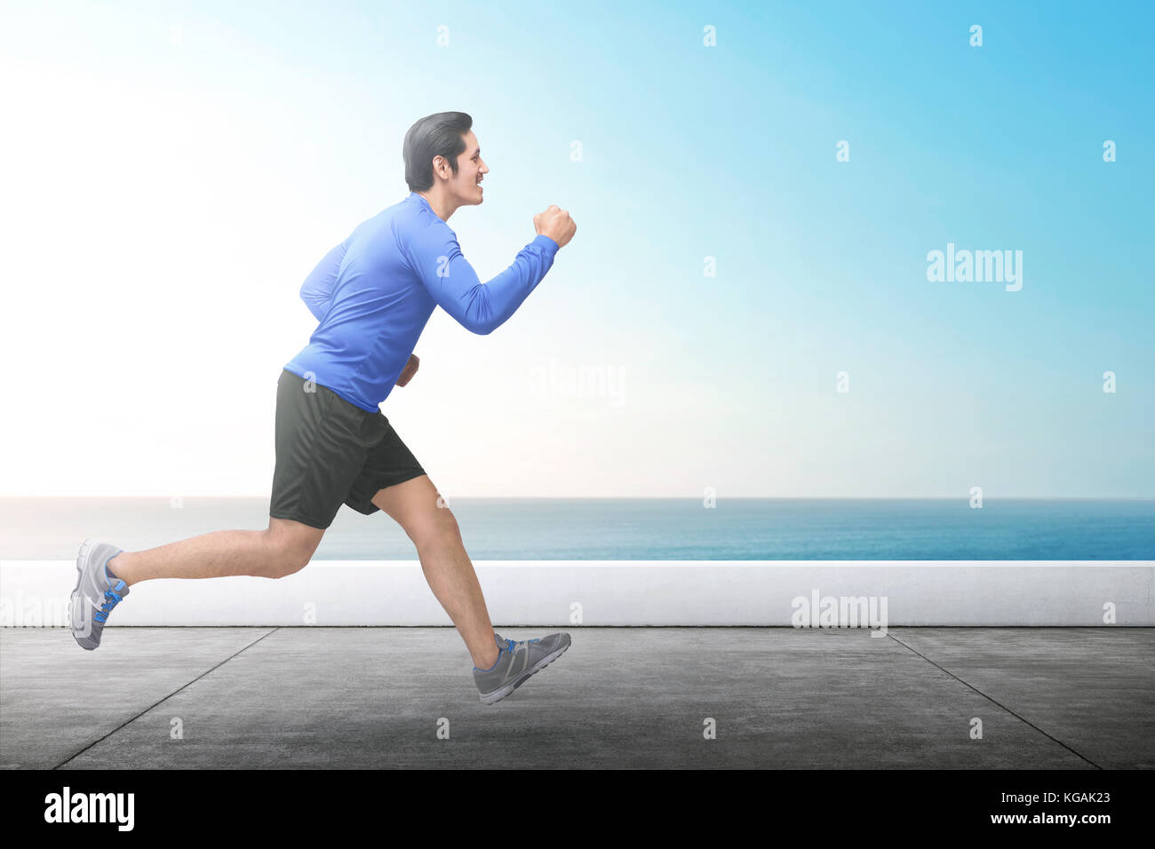 Young asian man in sportswear running on terrace with ocean background ...