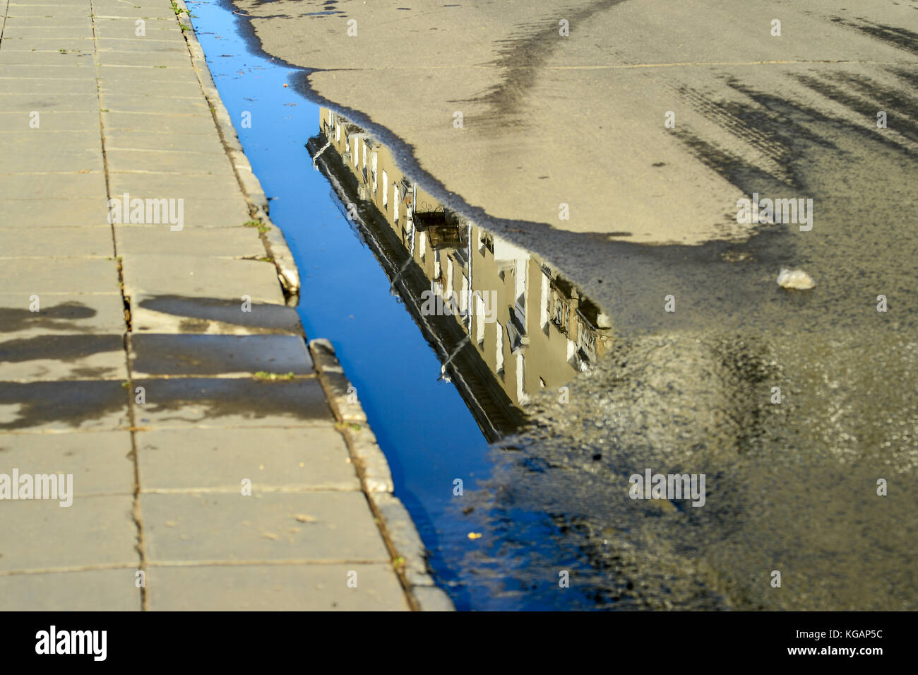 Water in a puddle on the roadside of an urban asphalt road with a ...