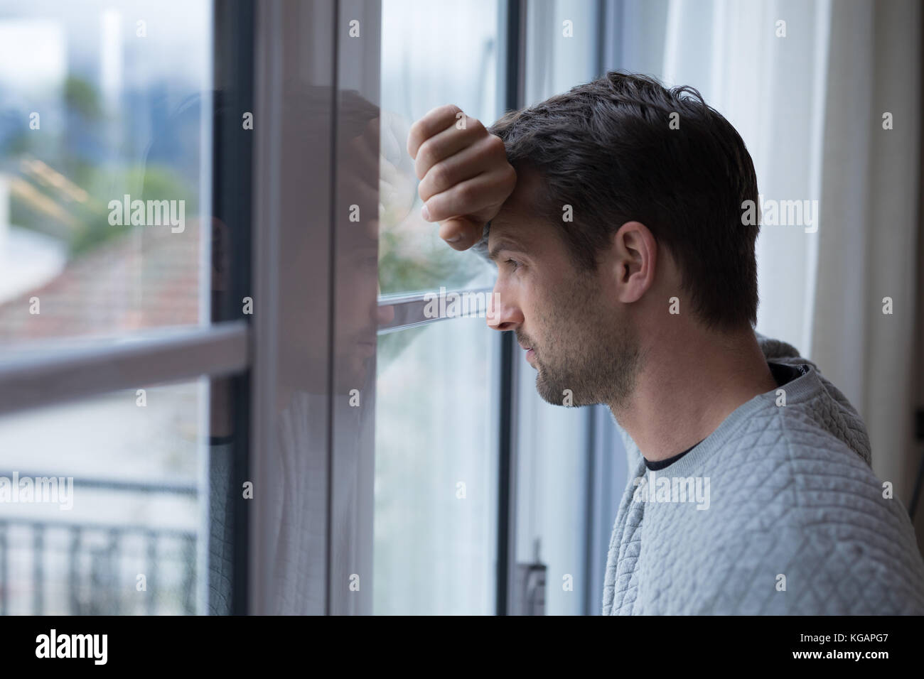 Thoughtful man looking through window at home Stock Photo - Alamy