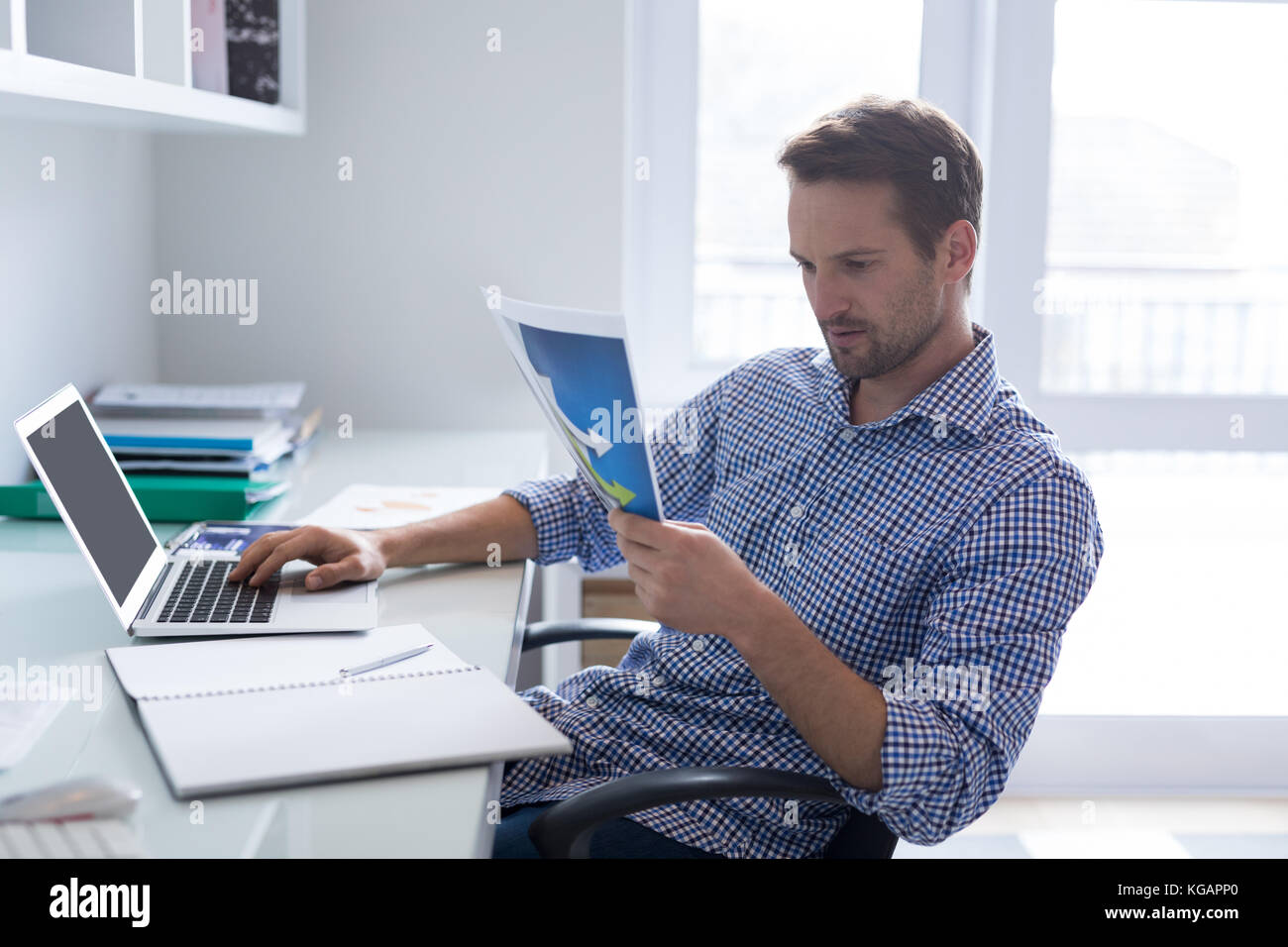 Man looking at graph while using laptop at desk Stock Photo - Alamy