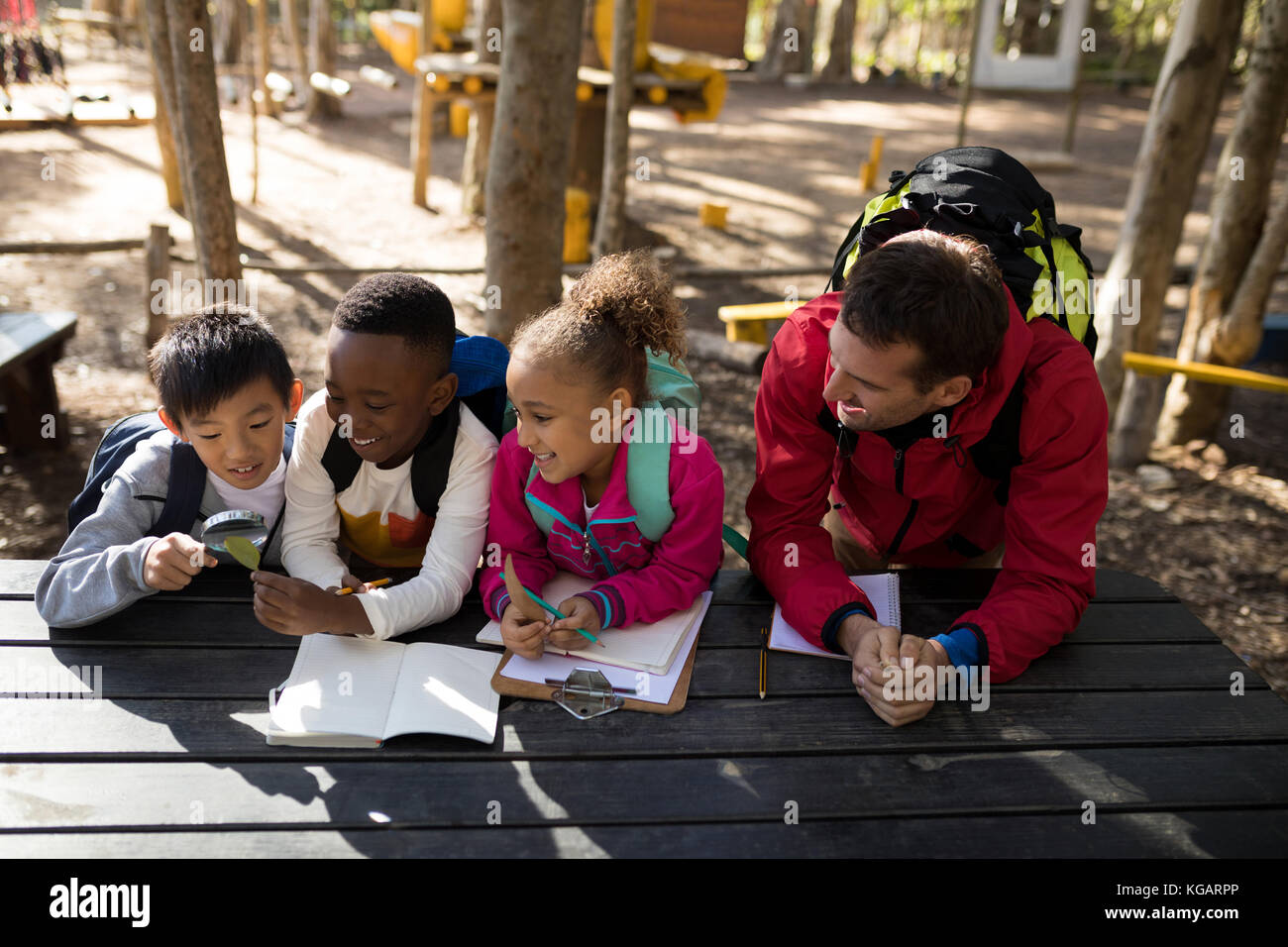 Teacher assisting kids in studying at park Stock Photo - Alamy
