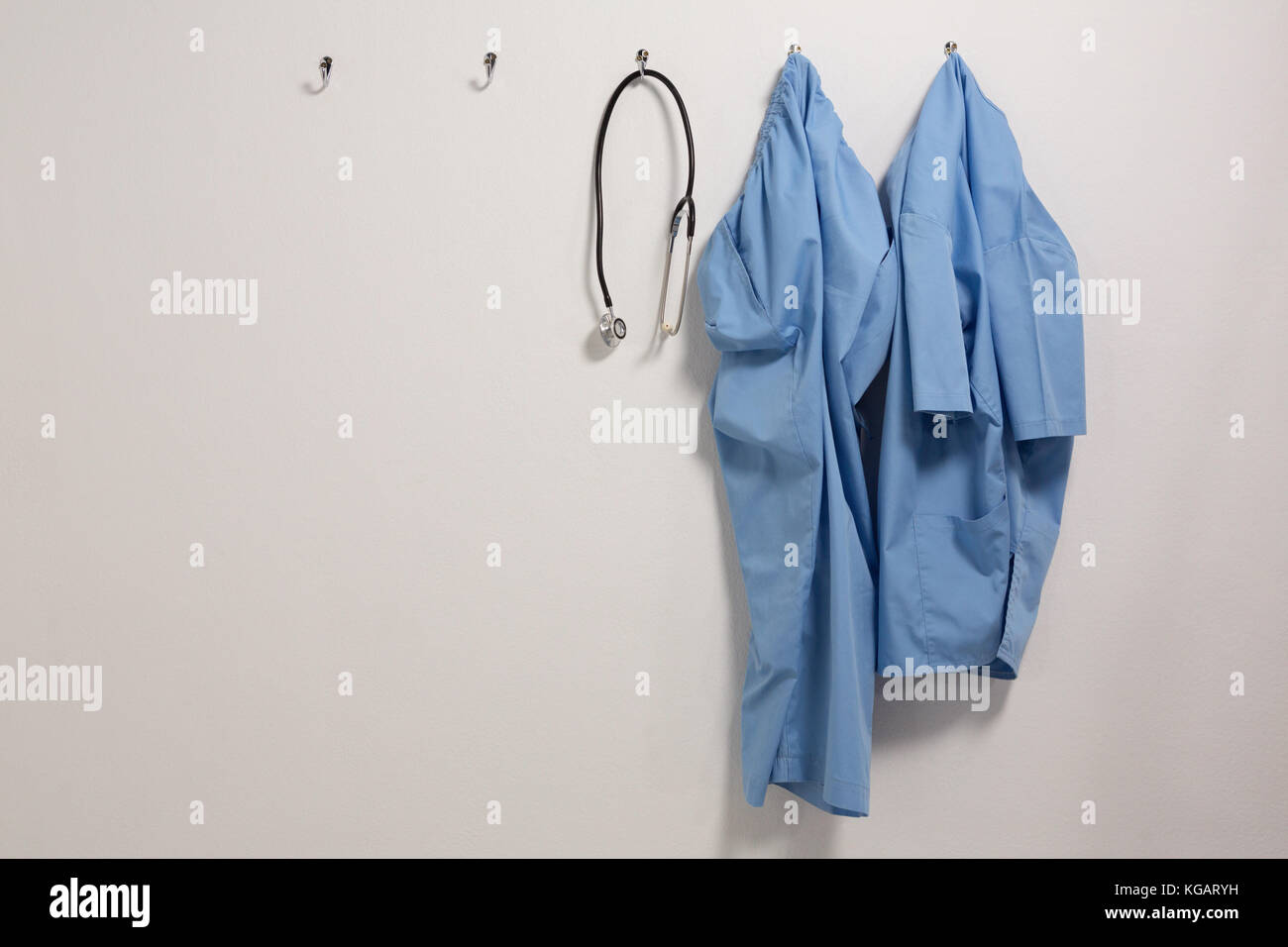 Scrubs and stethoscope hanging on hook against wall Stock Photo - Alamy