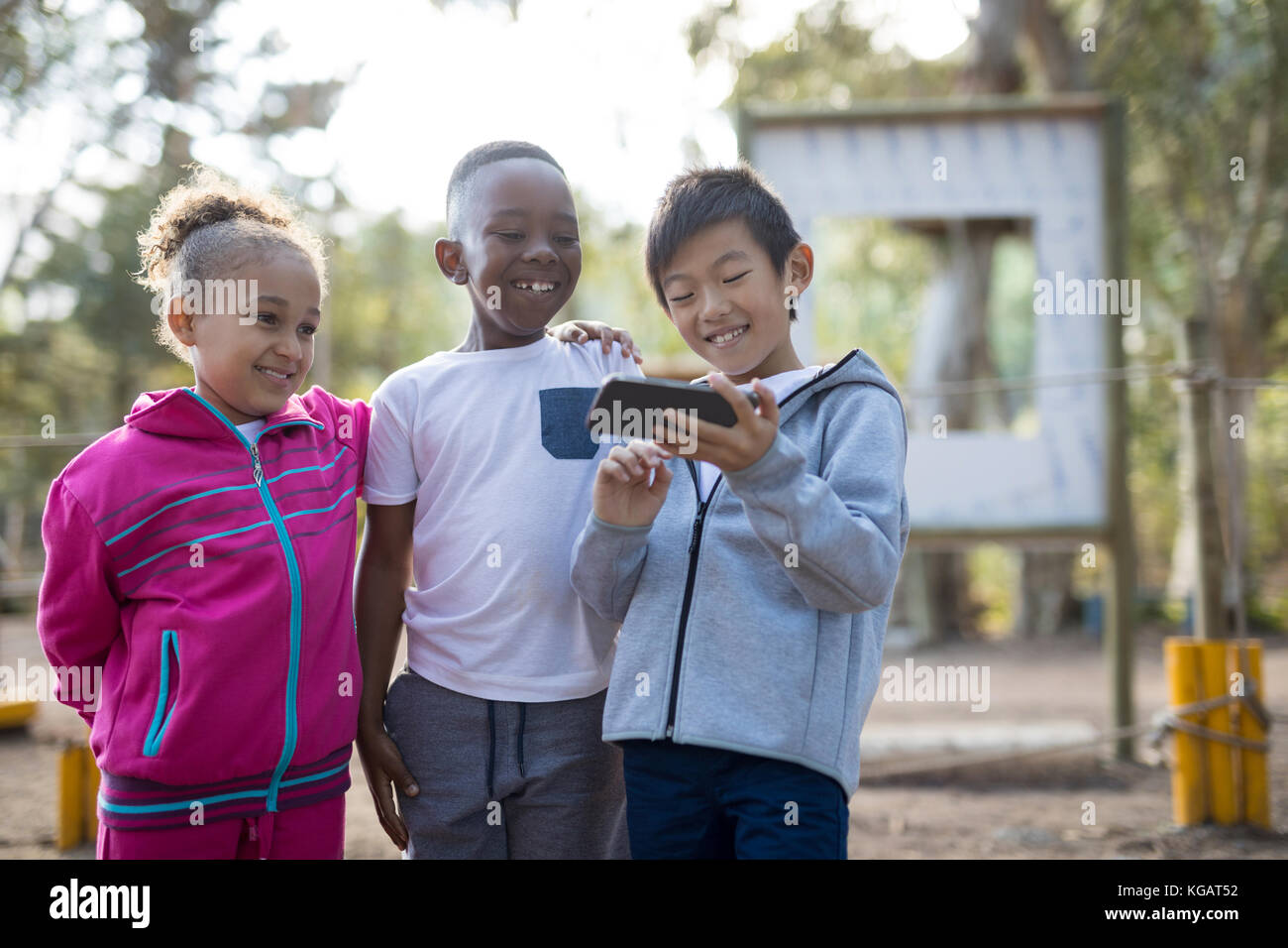 Happy kids using mobile phone in park Stock Photo - Alamy