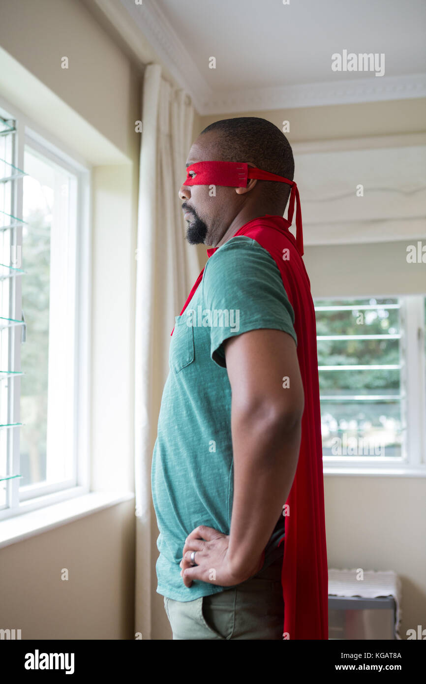 Man in superhero costume looking through window at home Stock Photo - Alamy