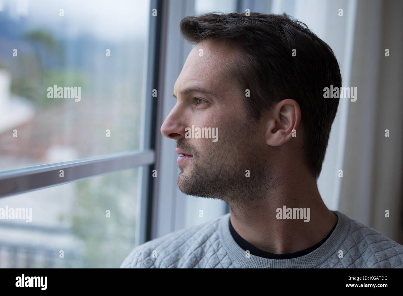 Thoughtful man looking through window at home Stock Photo - Alamy