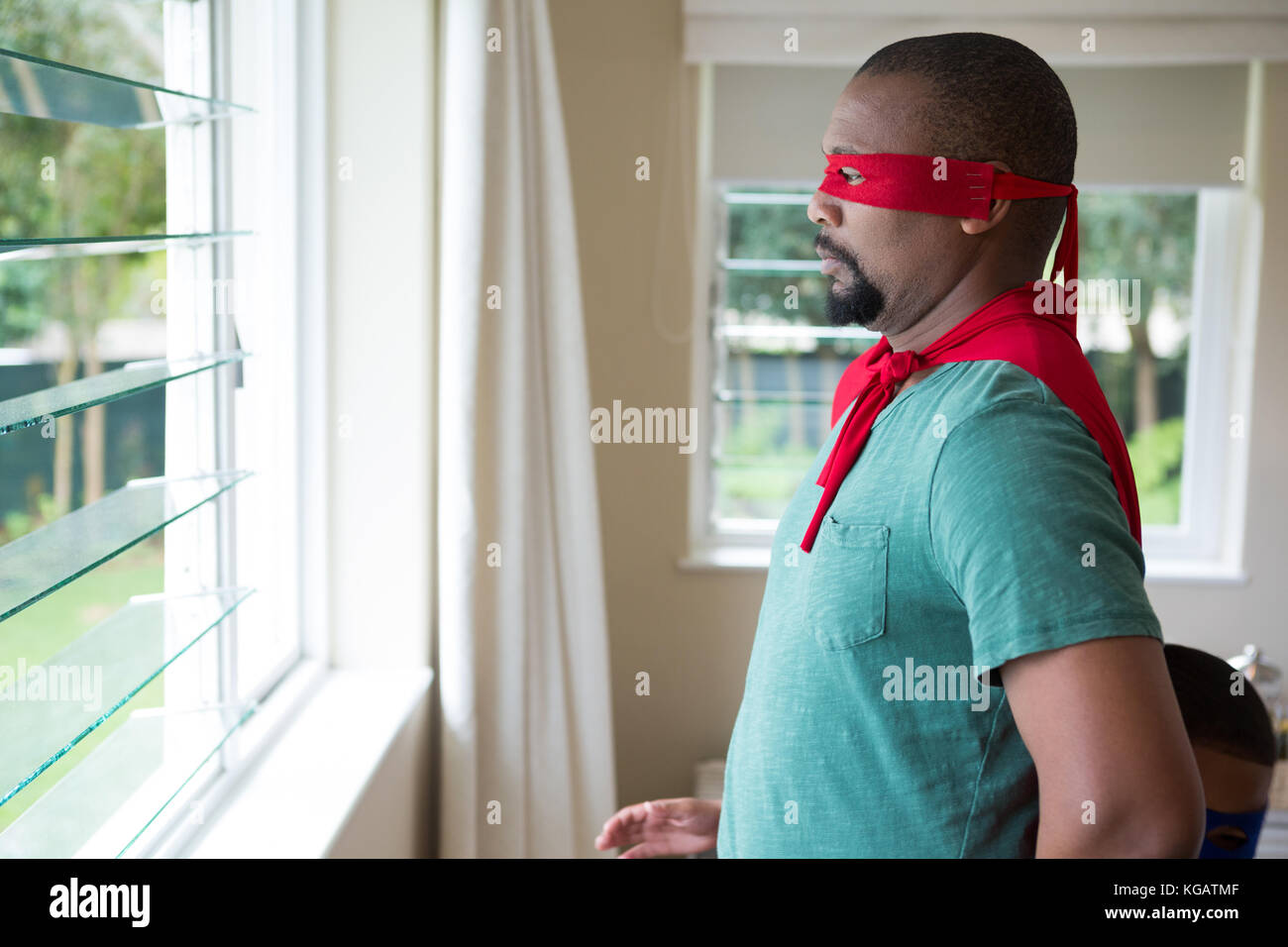 Man in superhero costume looking through window at home Stock Photo - Alamy